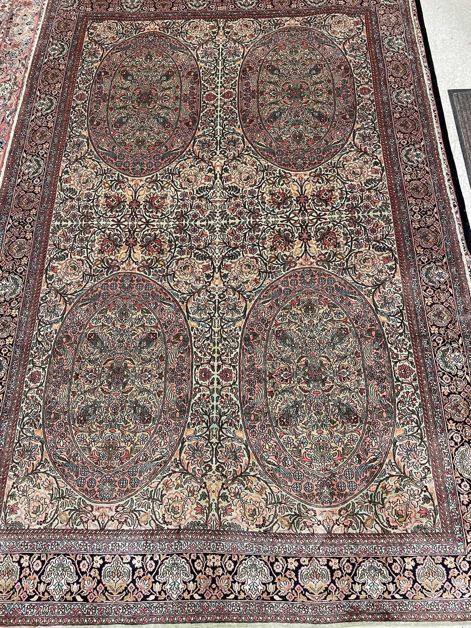 A persian silk rug, the pale green floral field with four oval guls ...