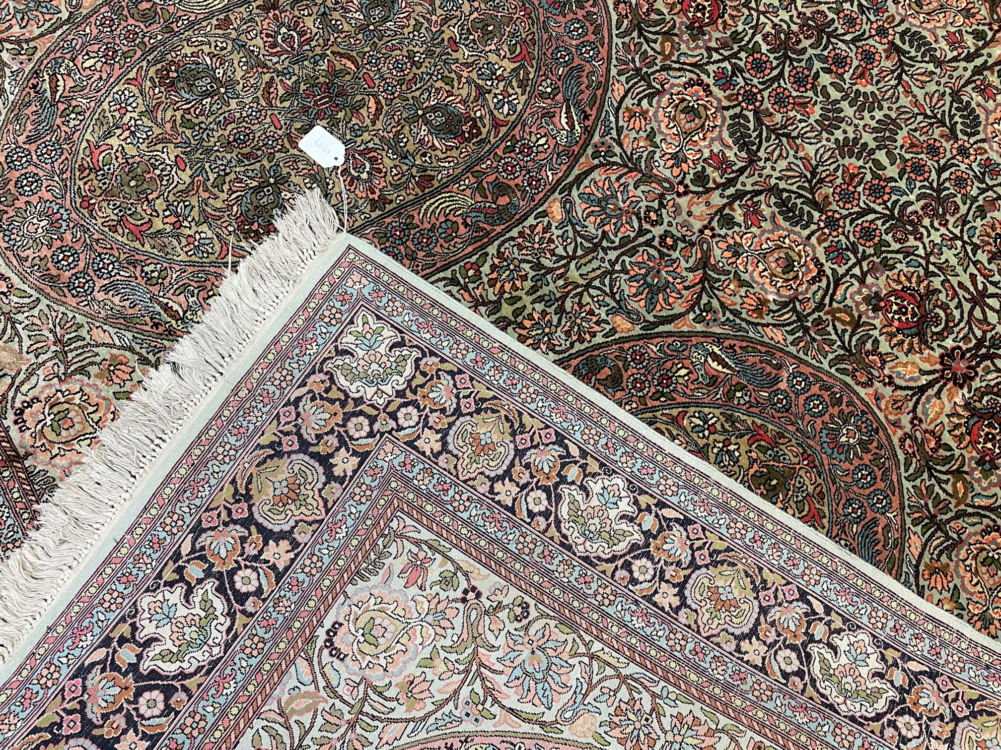 A persian silk rug, the pale green floral field with four oval guls ...
